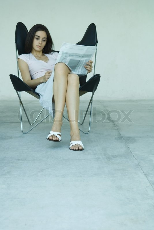 Young Woman Sitting In Chair With Legs Crossed Reading Newspaper Full