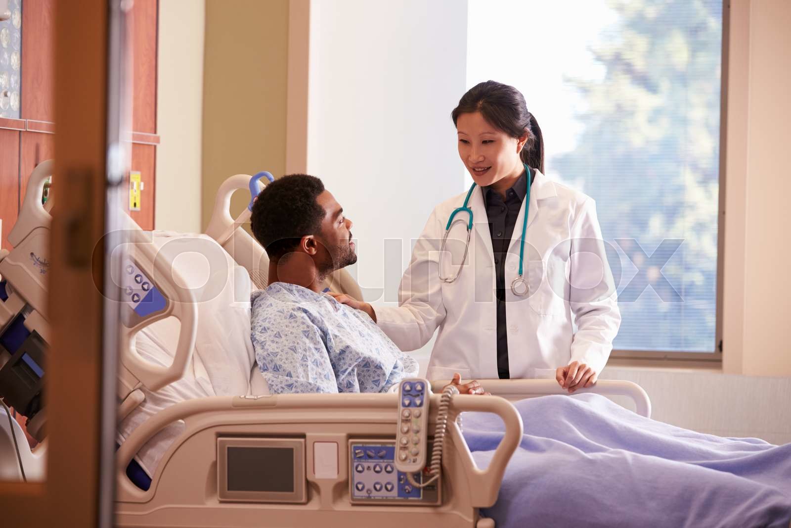 Female Doctor Talking To Male Patient In Hospital Bed Stock Image
