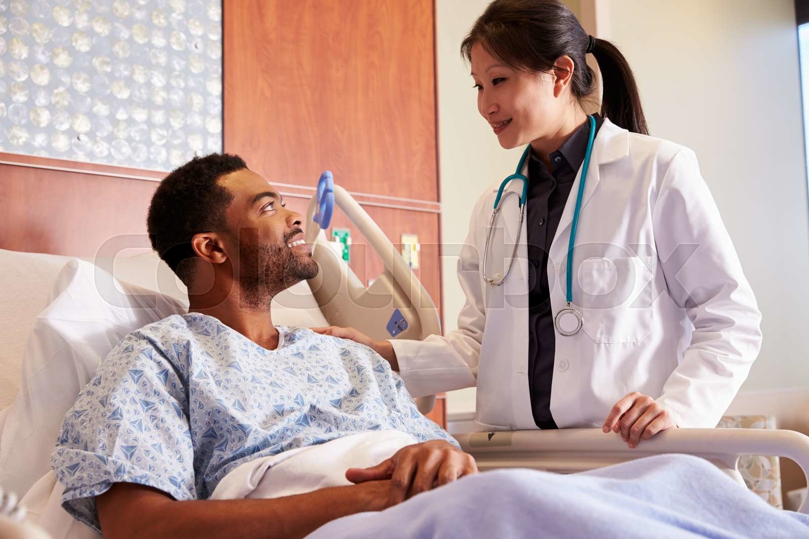 Female Doctor Talking To Male Patient In Hospital Bed Stock Image