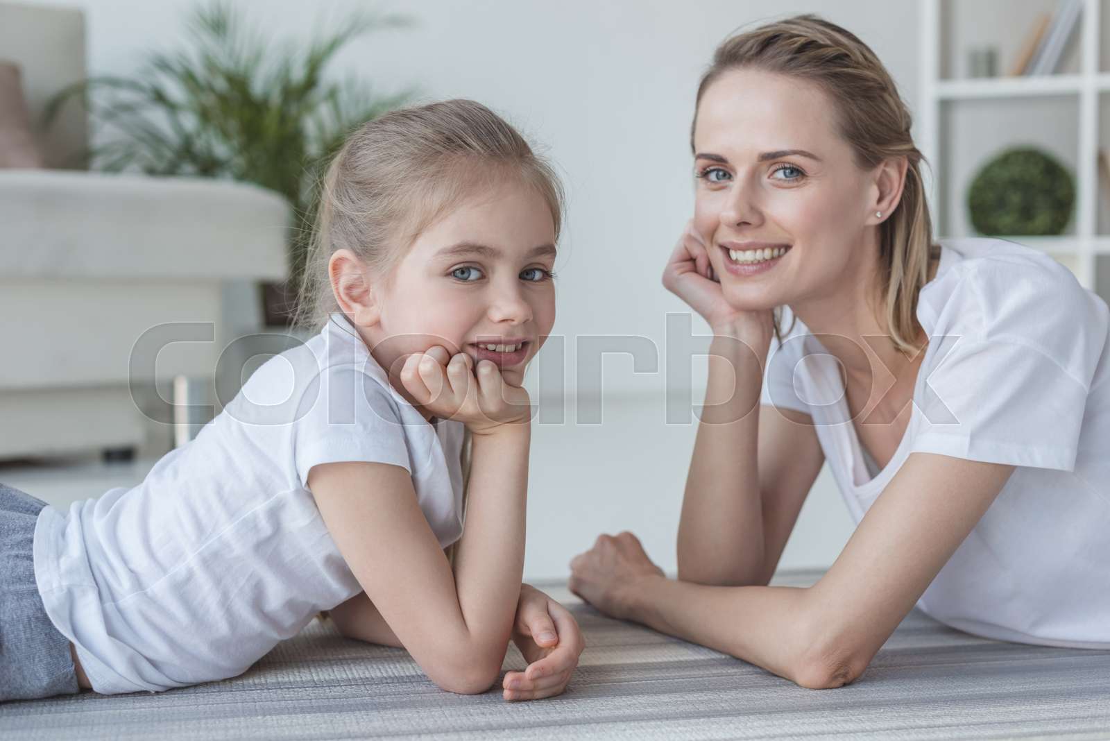 Mother And Daughter Lying On Floor Together And Looking At Camera