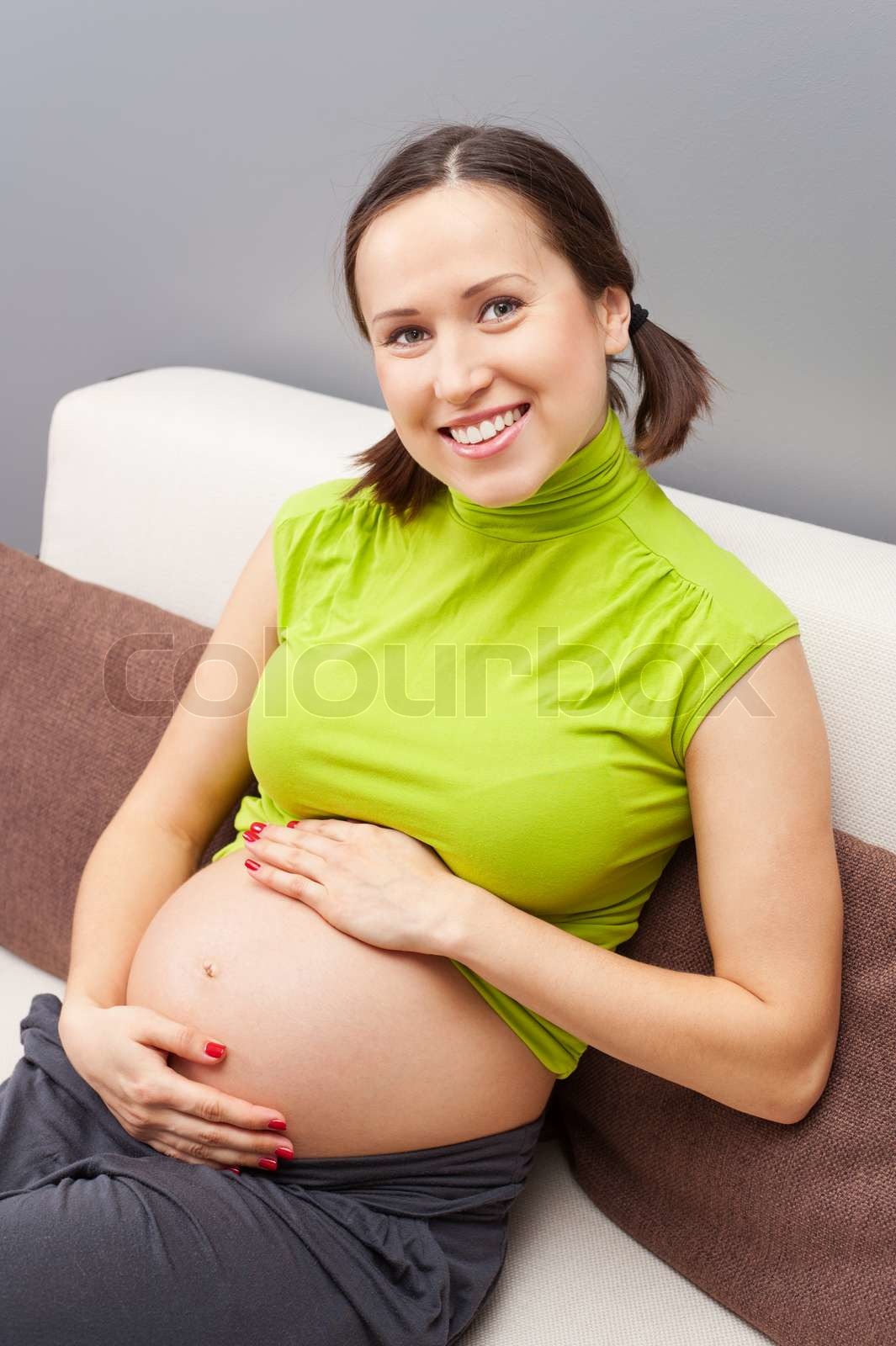 Happy Pregnant Woman Hug Her Belly And Sitting On Sofa Stock Image