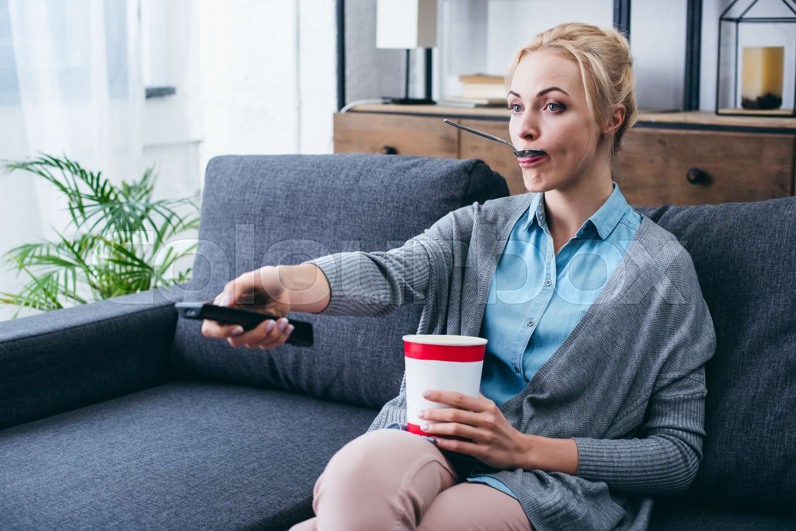 Woman Eating Ice Cream While Siitng On Couch And Wathicng Tv At Home