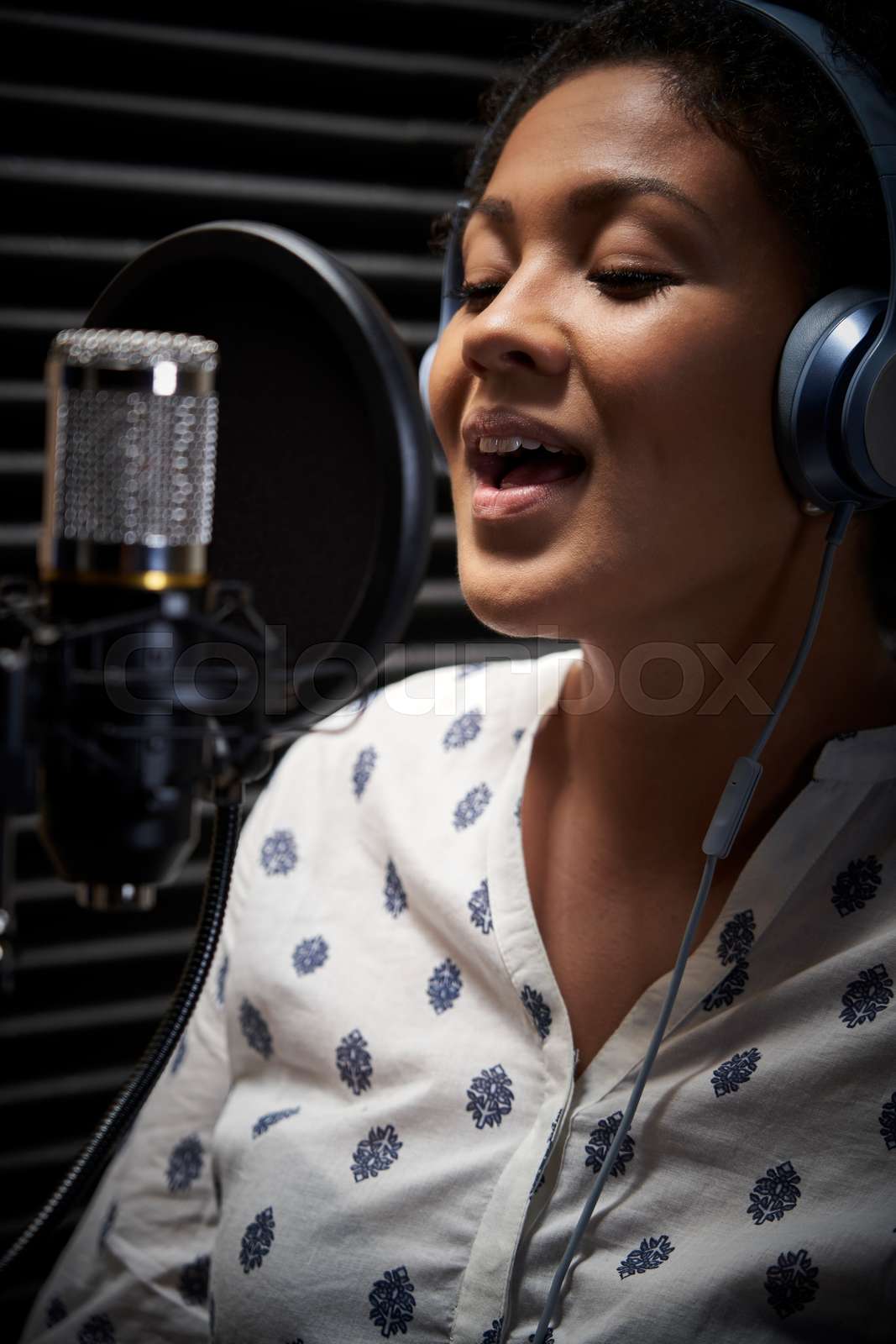 Female Vocalist Wearing Headphones Singing Into Microphone In Recording