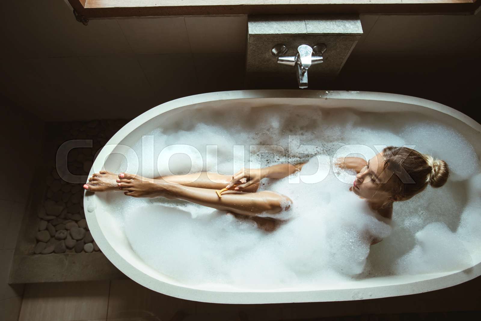 Woman Relaxing In Foam Bath With Bubbles In Dark Bathroom By Window