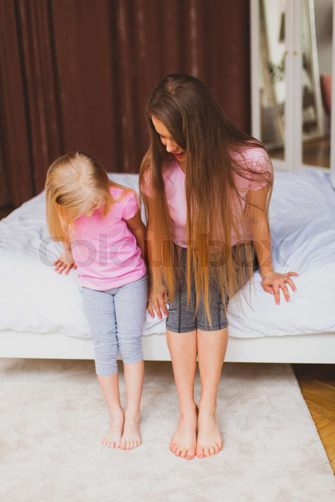 Young Mother And Daughter Sitting On A Bed Looking At Their Legs