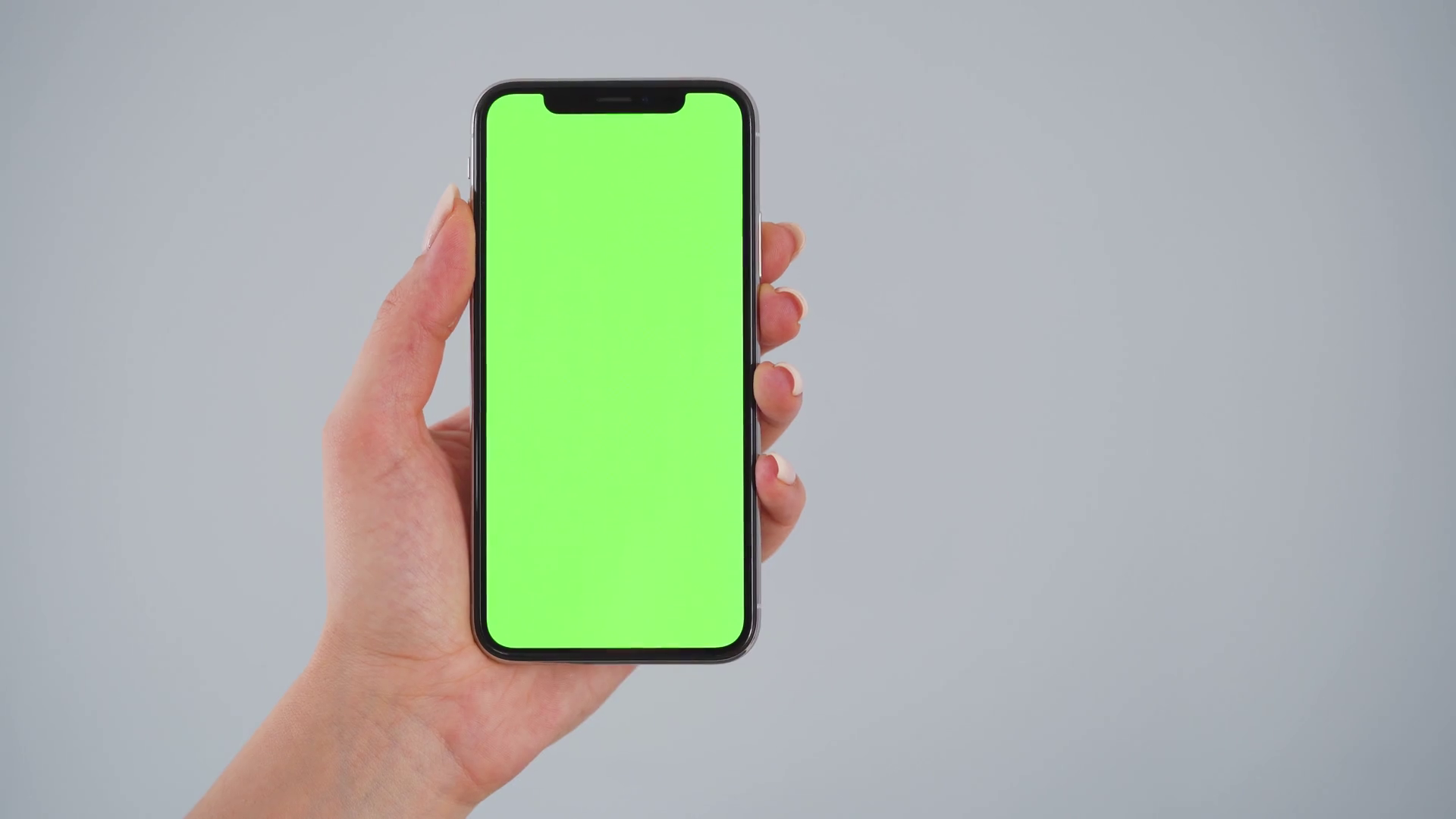 Female Hands Holding A Smartphone With A Green Screen On A Gray