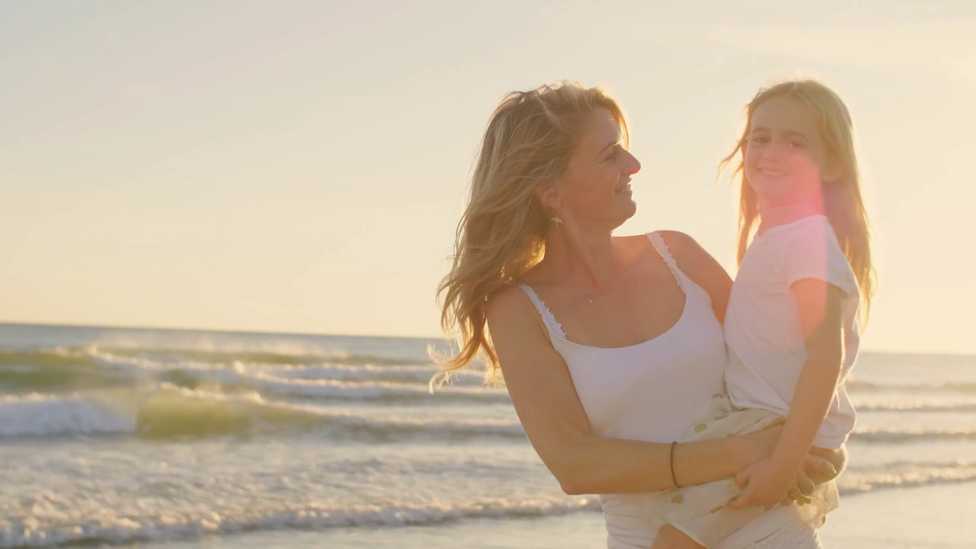 Mother And Daughter Standing On Beach Hugging And Playing In Sunset