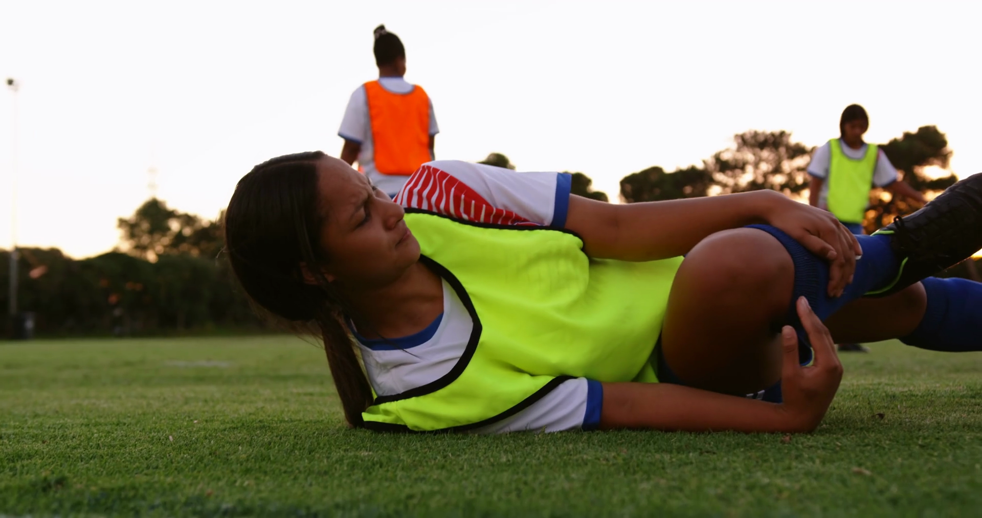 Injured Female Soccer Player Lying On The Ground And Getting Help From