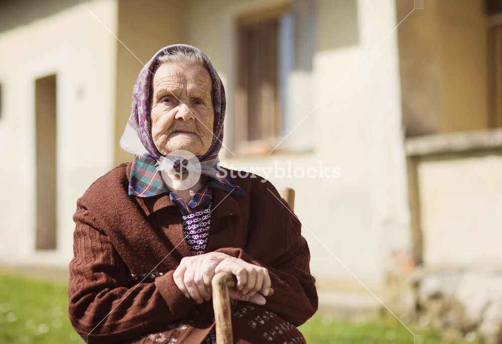 Very Old Woman With Head Scarf Sitting And Relaxing In The Garden