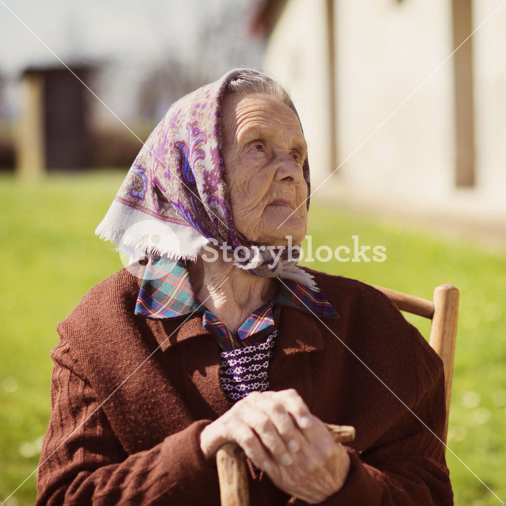 Very Old Woman With Head Scarf Sitting And Relaxing In The Garden