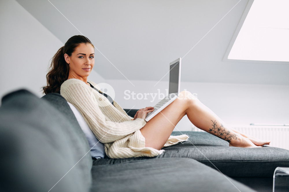 Portrait Of Young Woman On A Couch With A Laptop Looking At Camera