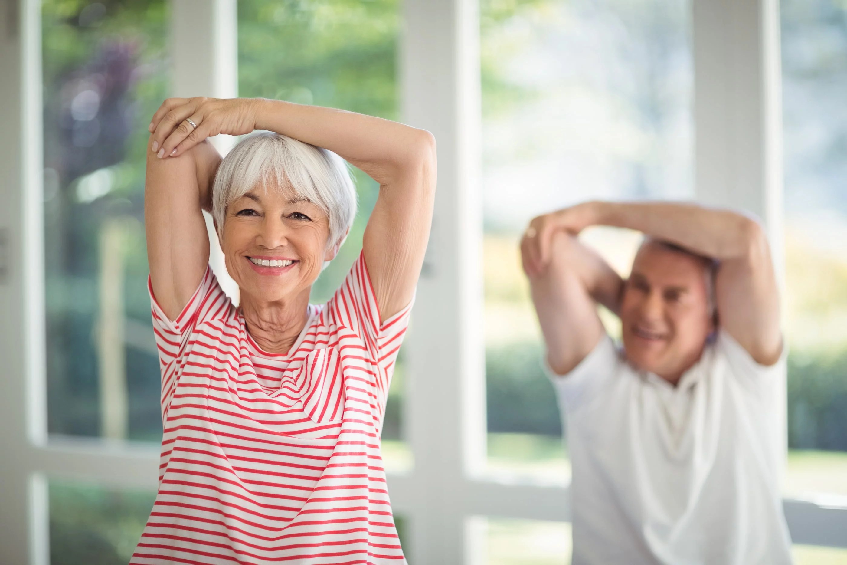 Happy Senior Couple Performing Stretching Exercise At Home Omni Fitt